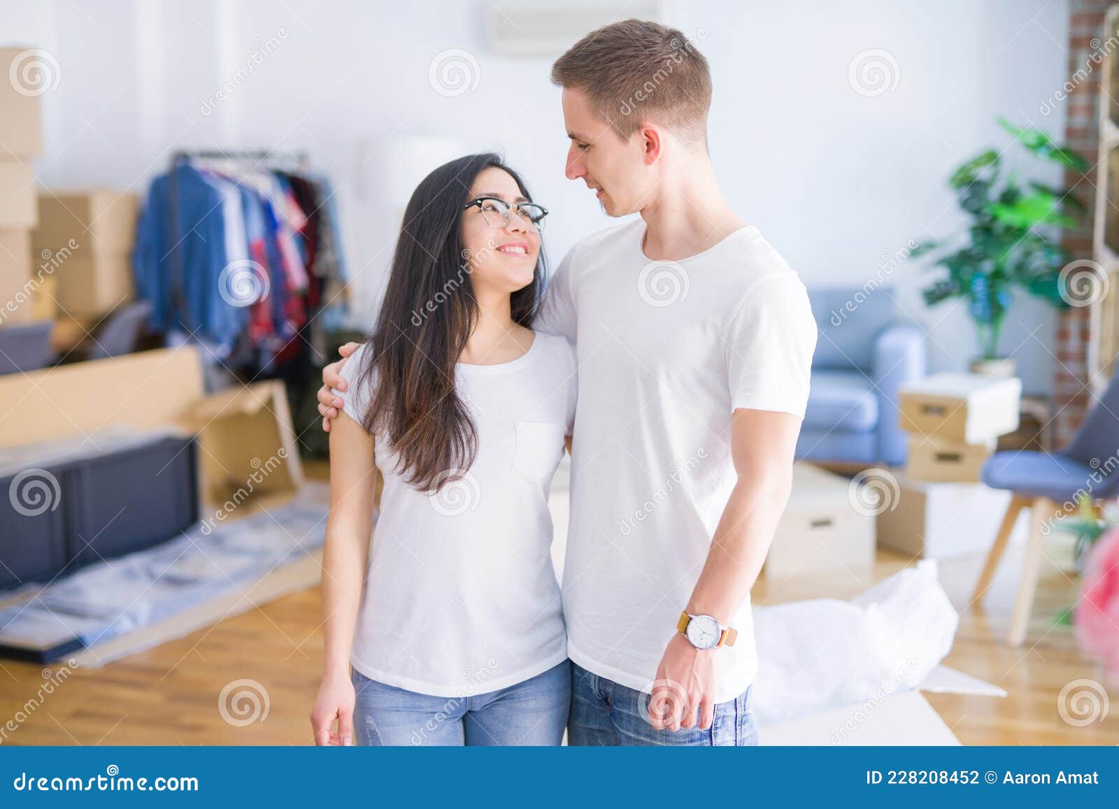 Young Beautiful Couple Standing At New Home Around Cardboard Boxes