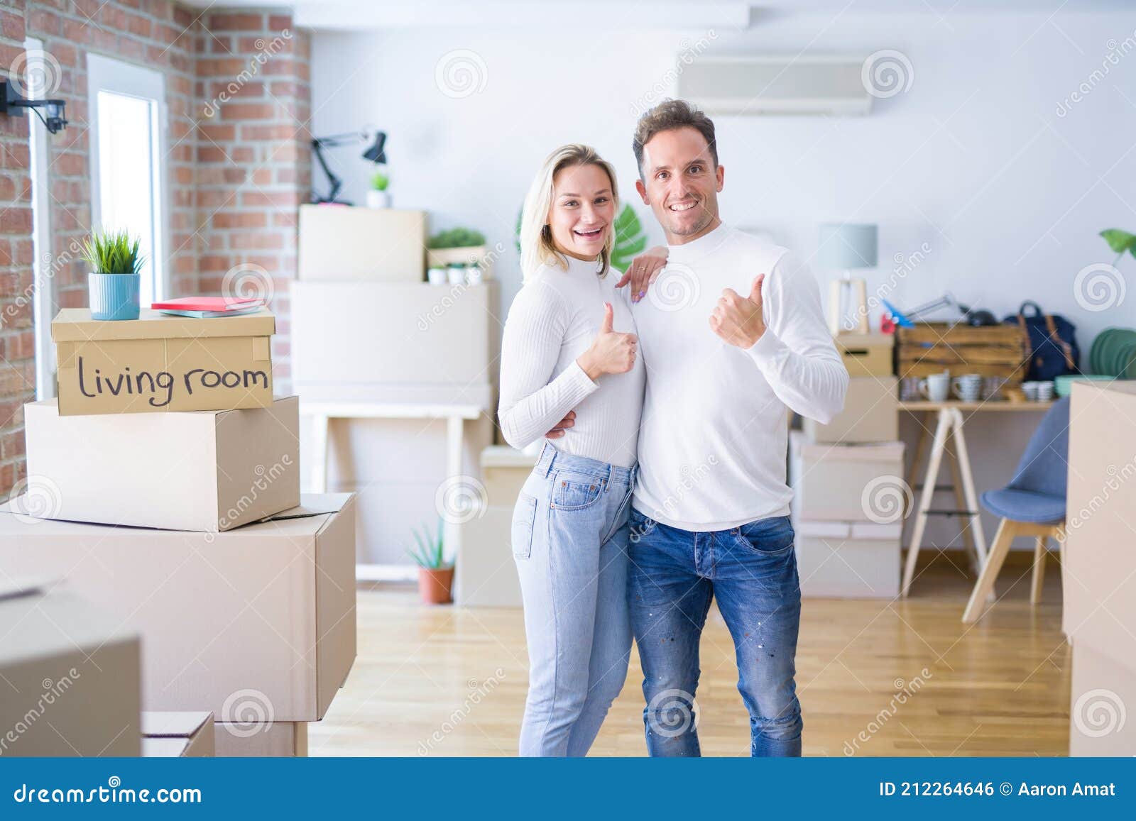 Young Beautiful Couple Standing At New Home Around Cardboard Boxes