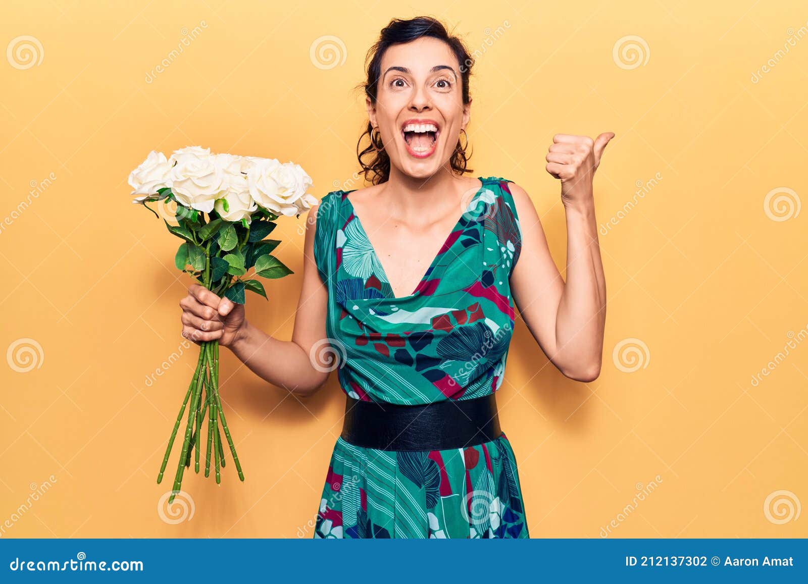 Young Beautiful Hispanic Woman Holding Flowers Pointing Thumb Up To The