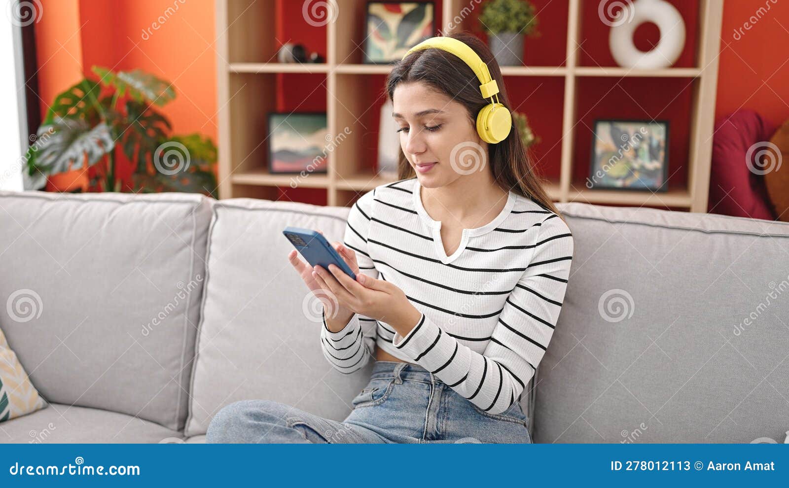 Young Beautiful Hispanic Woman Listening To Music Sitting On Sofa At