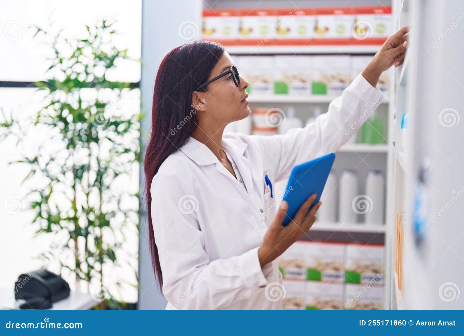 Young Beautiful Hispanic Woman Pharmacist Using Touchpad Working at ...