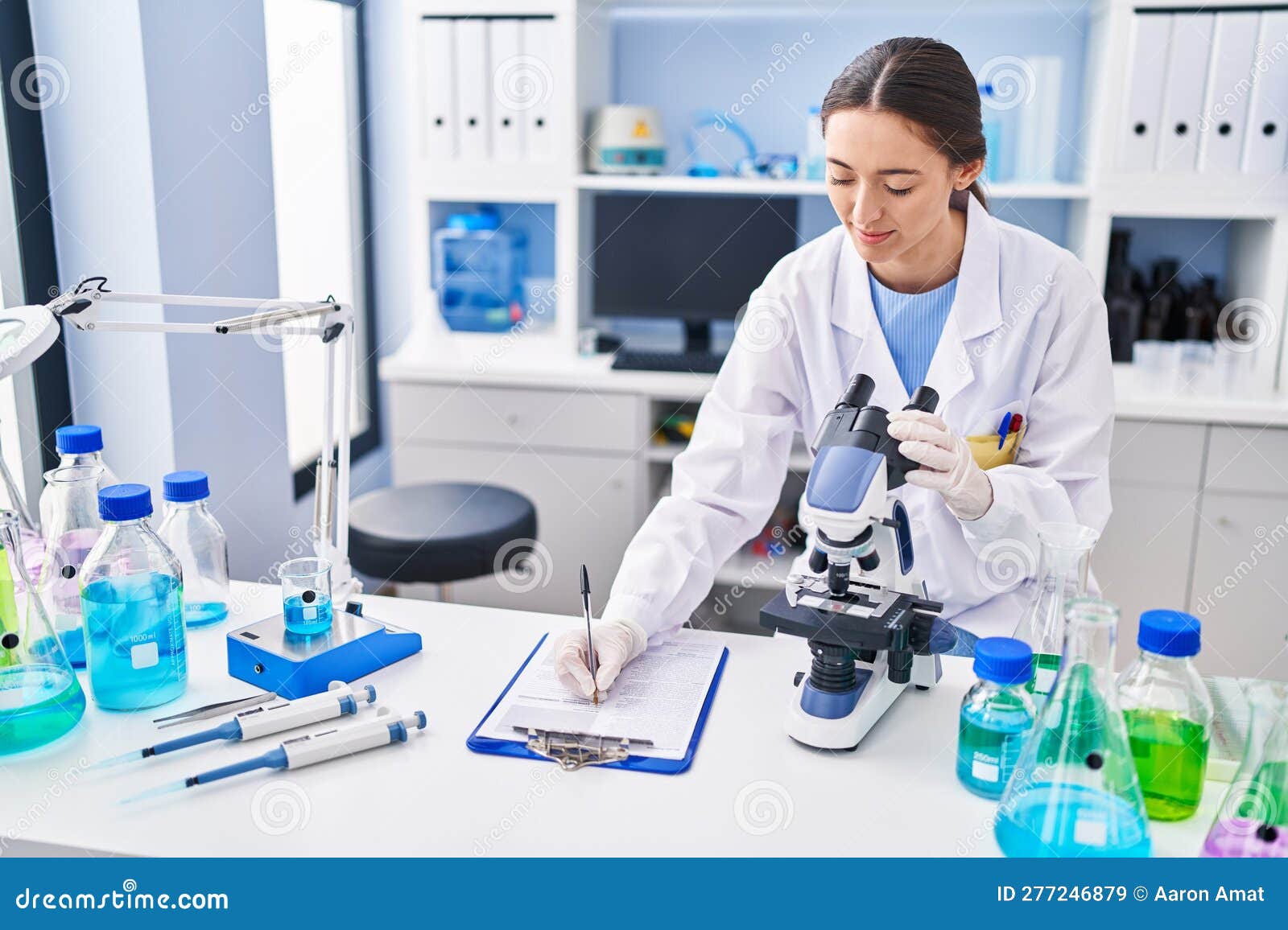 Young Beautiful Hispanic Woman Scientist Using Microscope Writing on ...