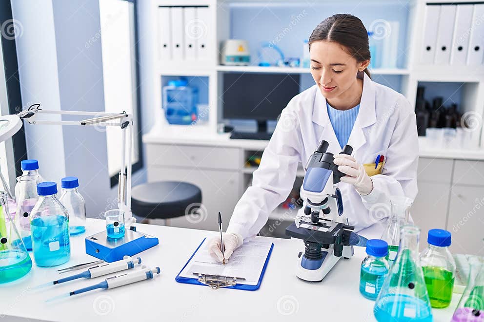 Young Beautiful Hispanic Woman Scientist Using Microscope Writing on ...