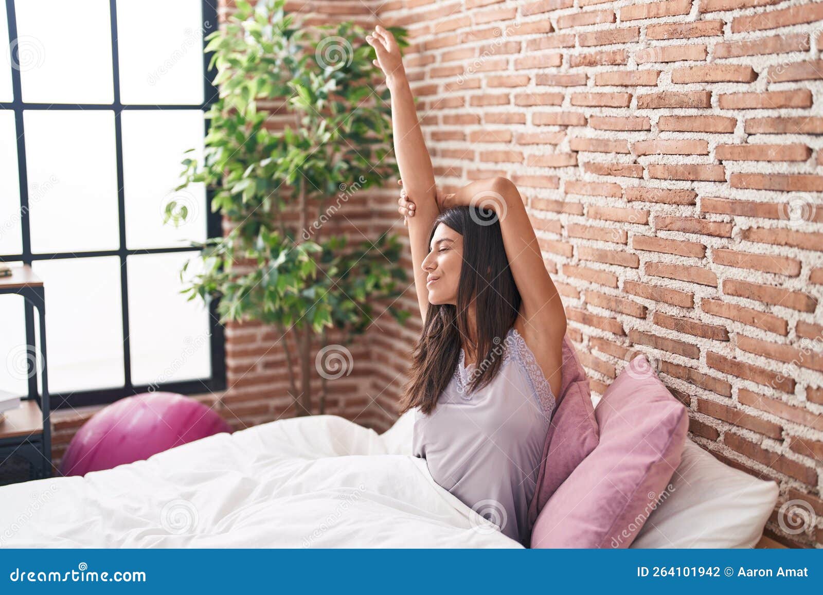 Young Beautiful Hispanic Woman Waking Up Stretching Arms At Bedroom