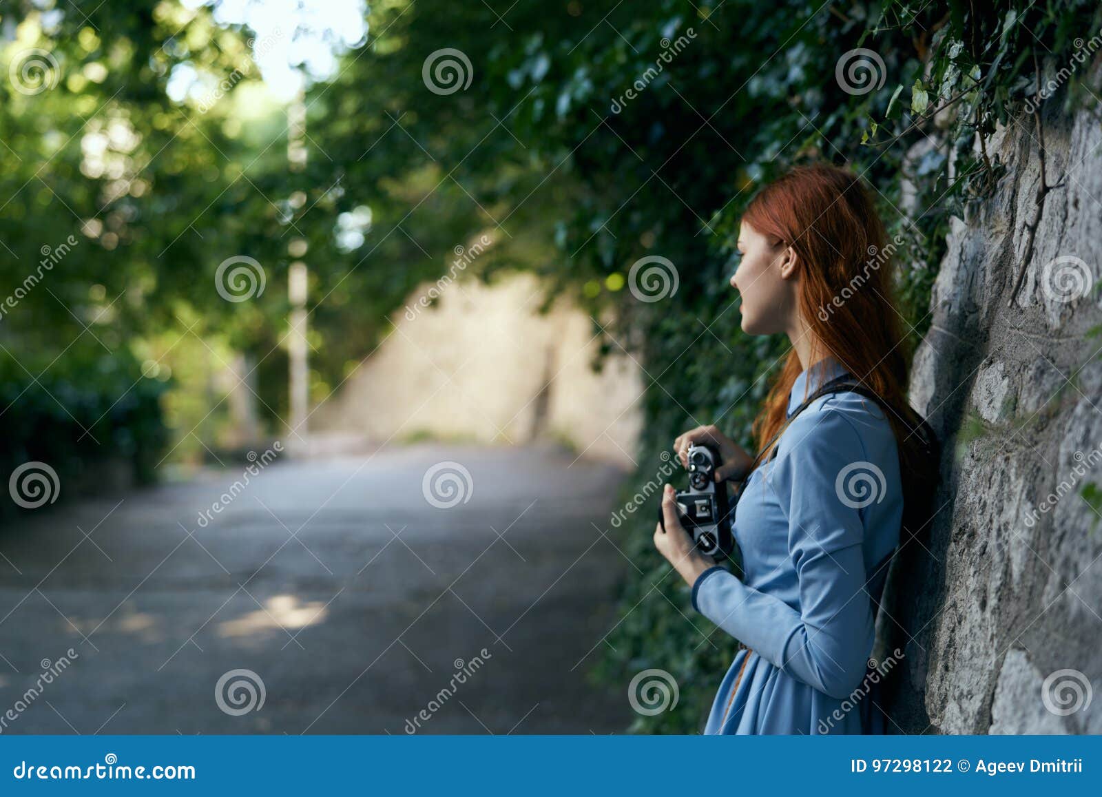 Young Beautiful Woman In A Blue Dress Is Holding A Camera On The Street