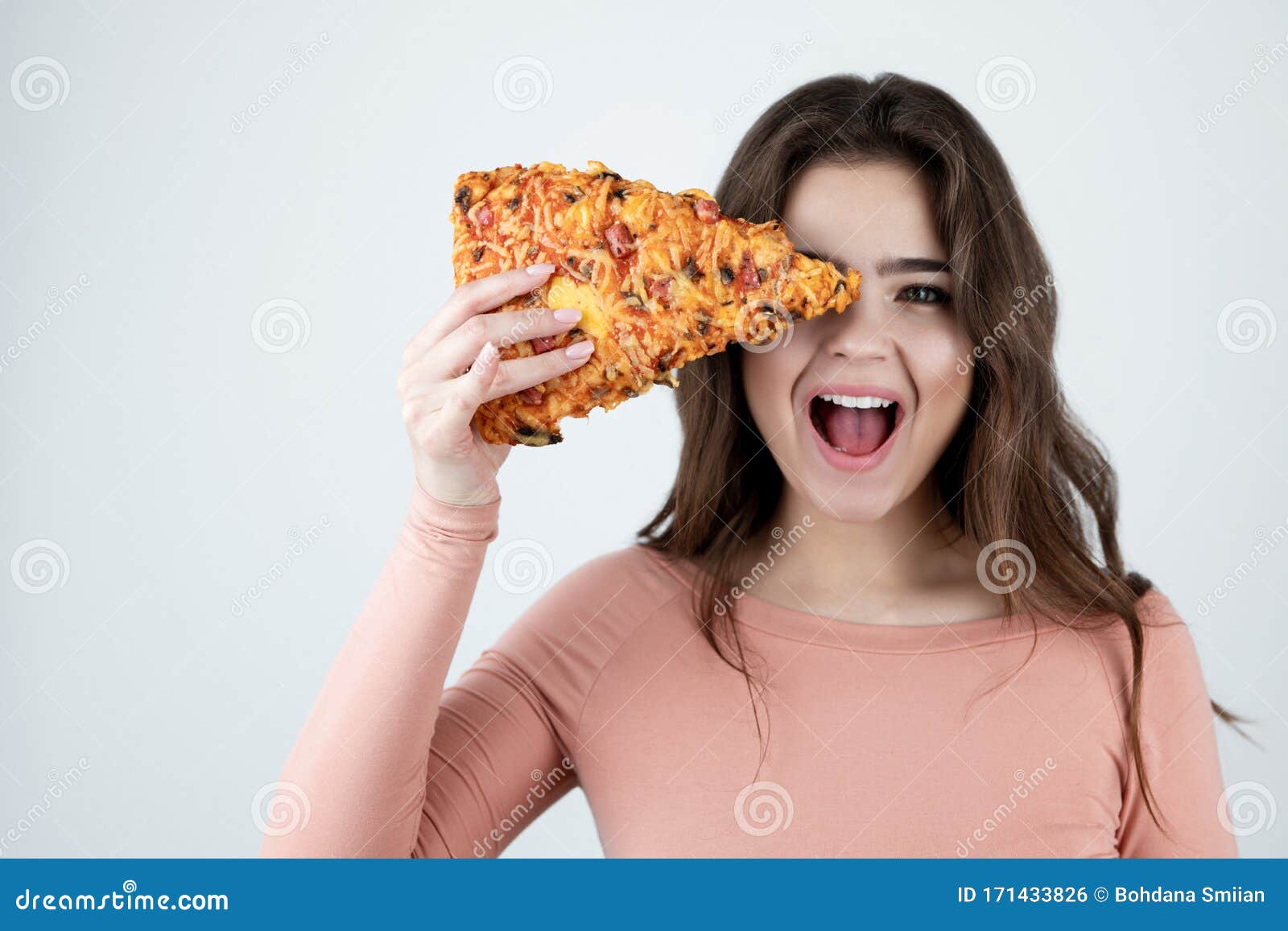 Young Beautiful Woman Holding Slice Of Pizza In One Hand Near Her Face