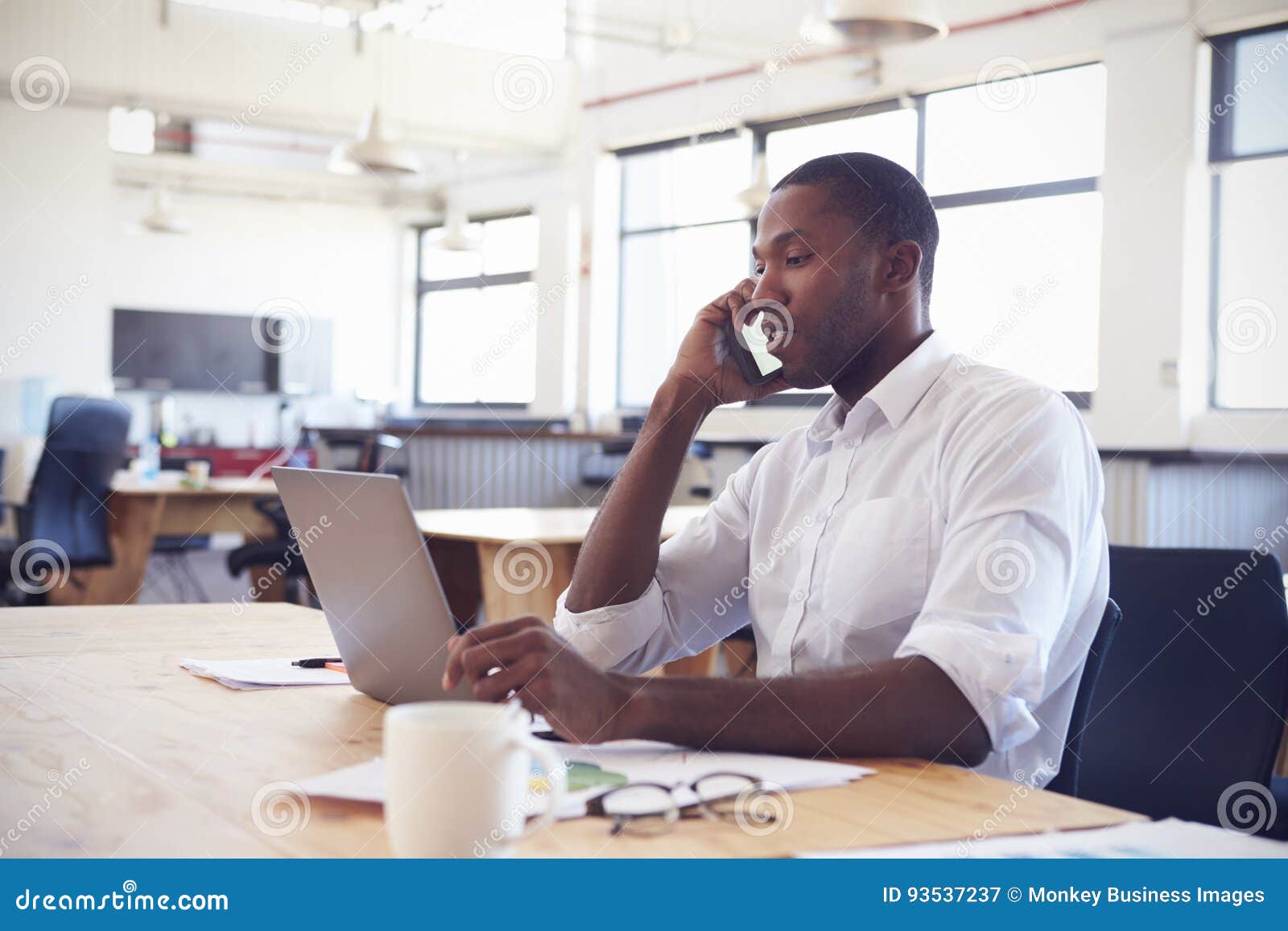 Young Black Man Working in Office with Laptop Using Phone Stock Image ...