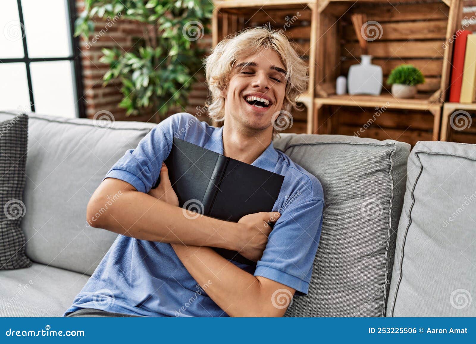 Young Blond Man Hugging Book Sitting on Sofa at Home Stock Photo ...