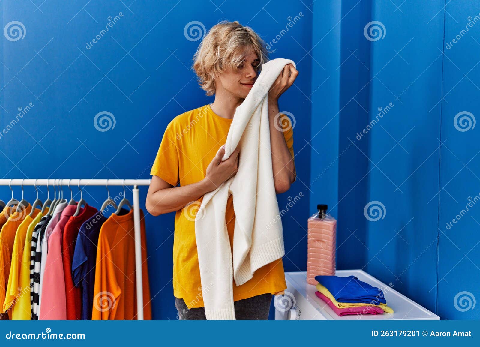 Young Blond Man Smiling Confident Smelling Clothes at Laundry Room ...