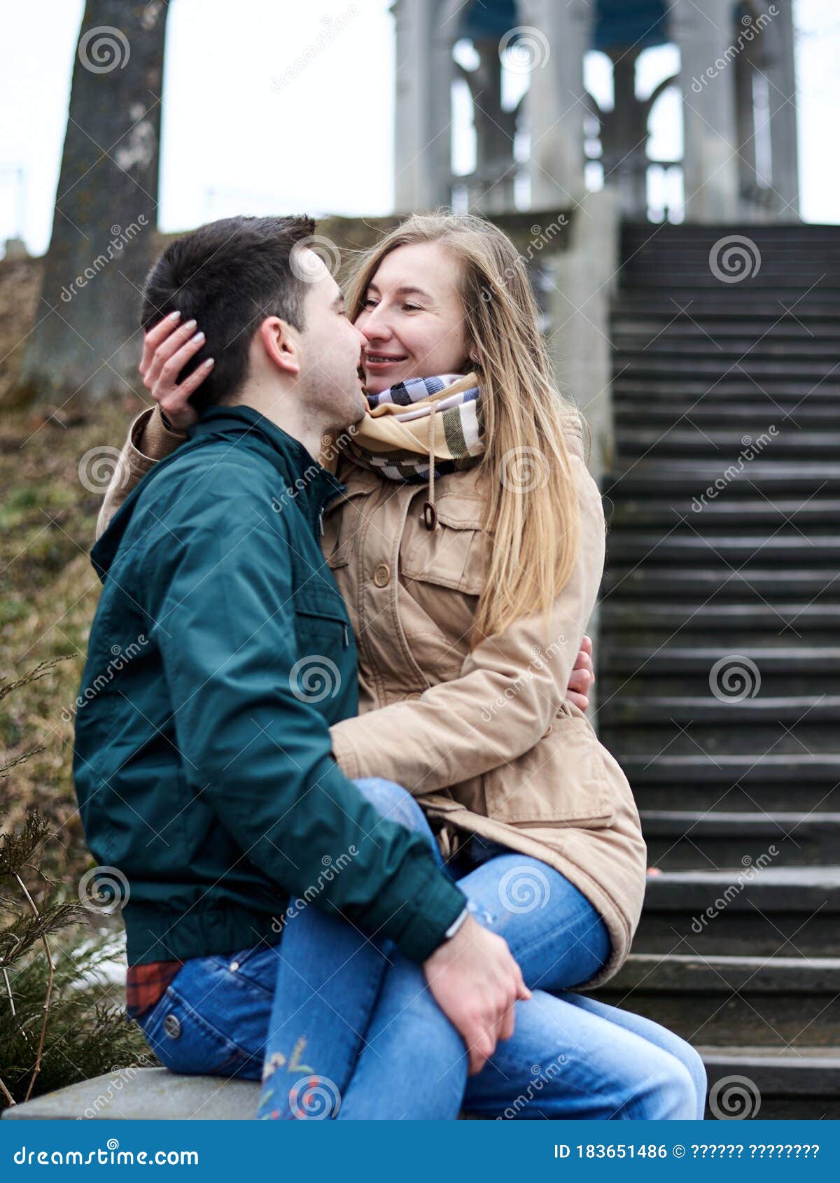 Young Blond Woman Is Sitting On Brunette Man`s Lap Hugging Each Other