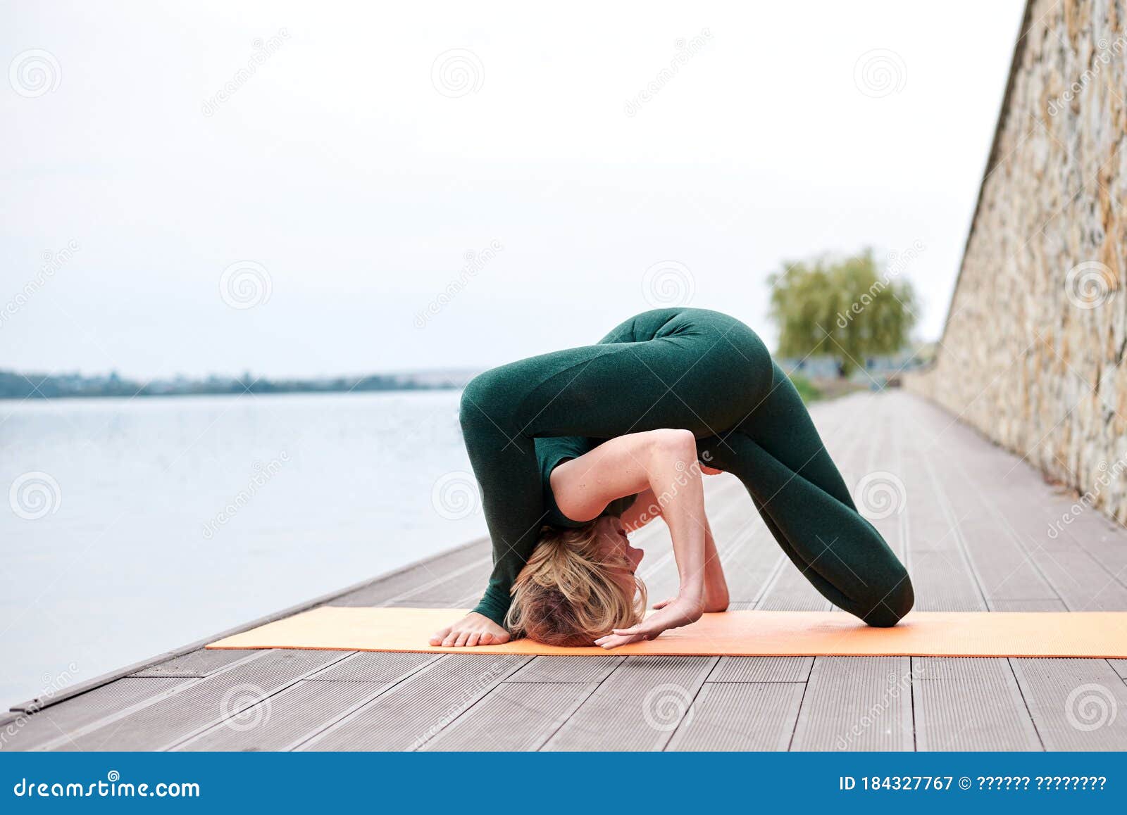Young Blond Woman Wearing Green Overall With Bare Feet Doing Yoga Pose