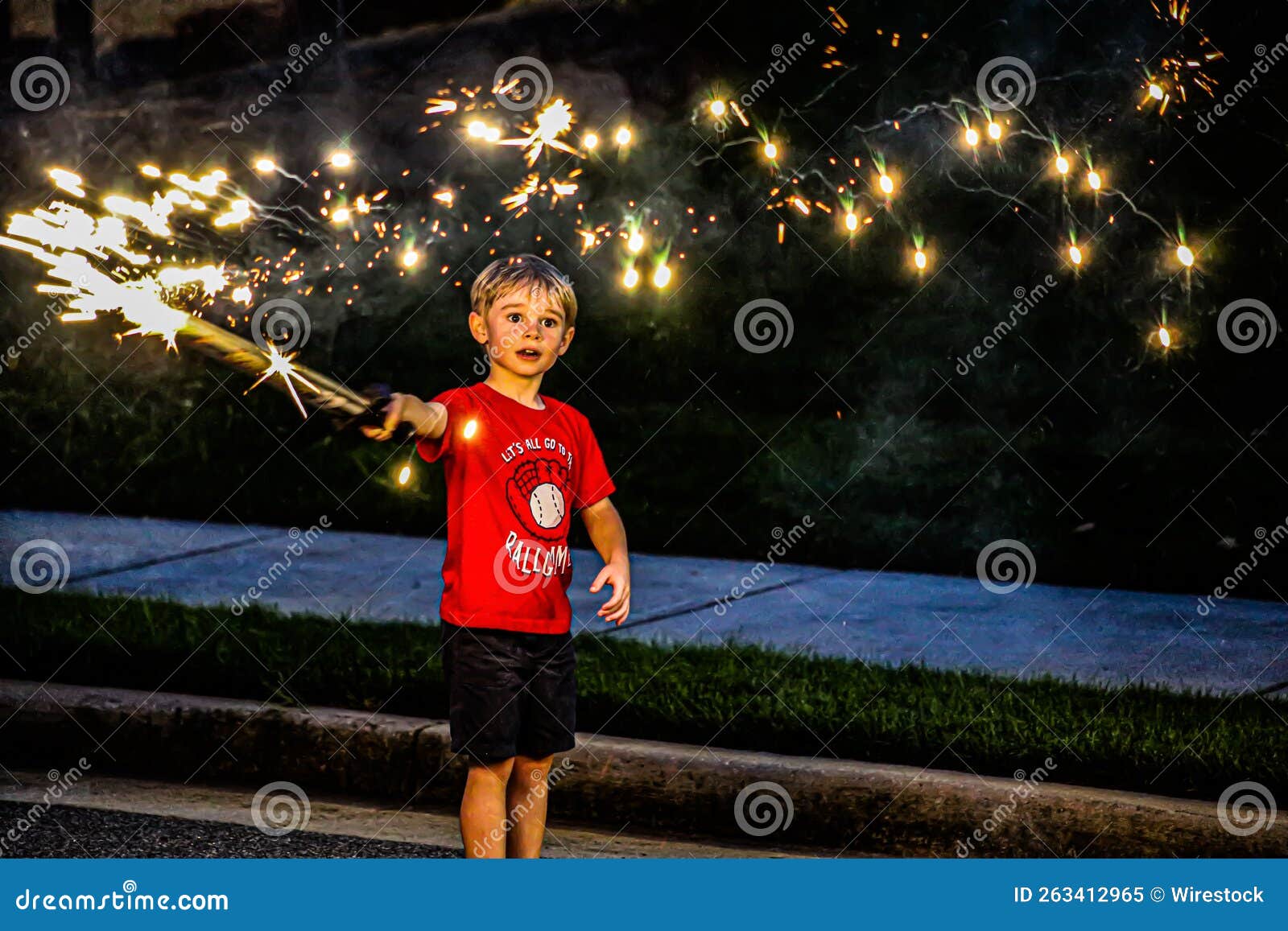 Young Blonde Boy Looking at Fireworks while Holding a Firecracker on ...