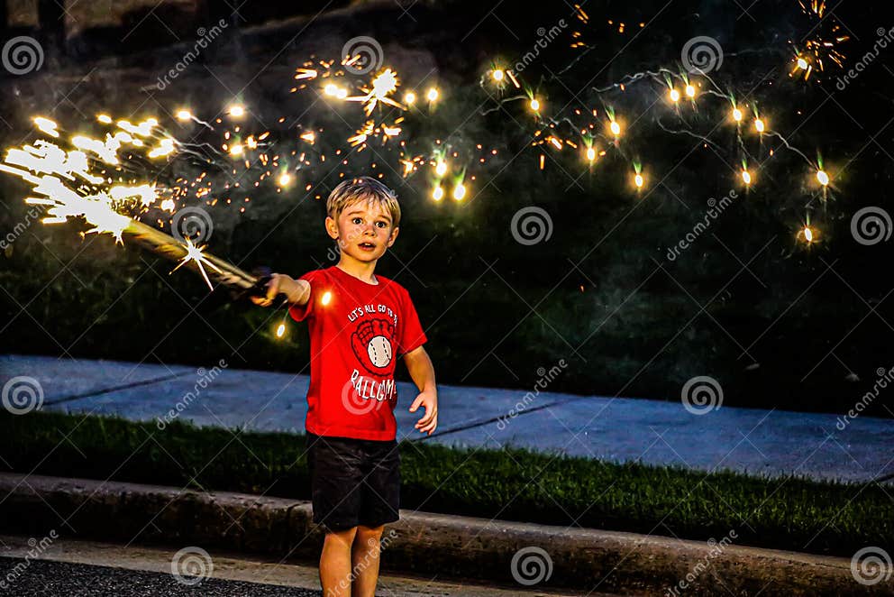 Young Blonde Boy Looking at Fireworks while Holding a Firecracker on ...