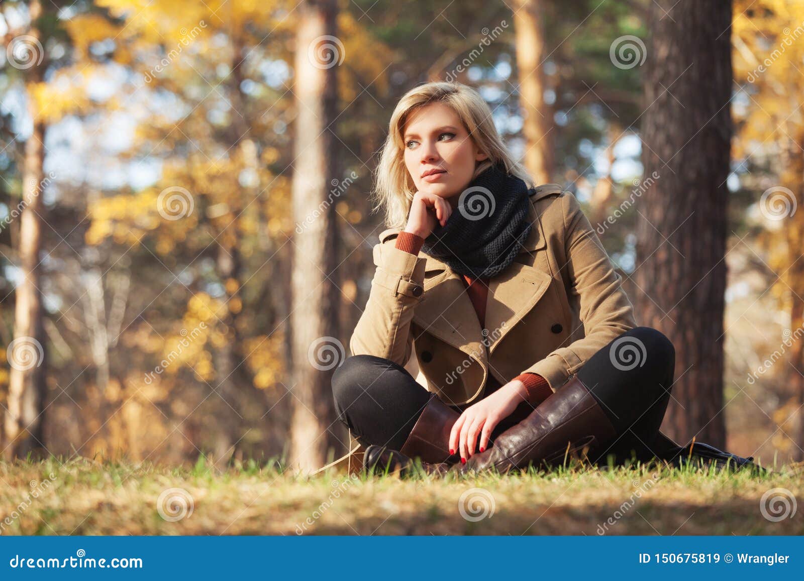 Young Fashion Woman In Beige Coat Sitting On Grass In Autumn Park Stock