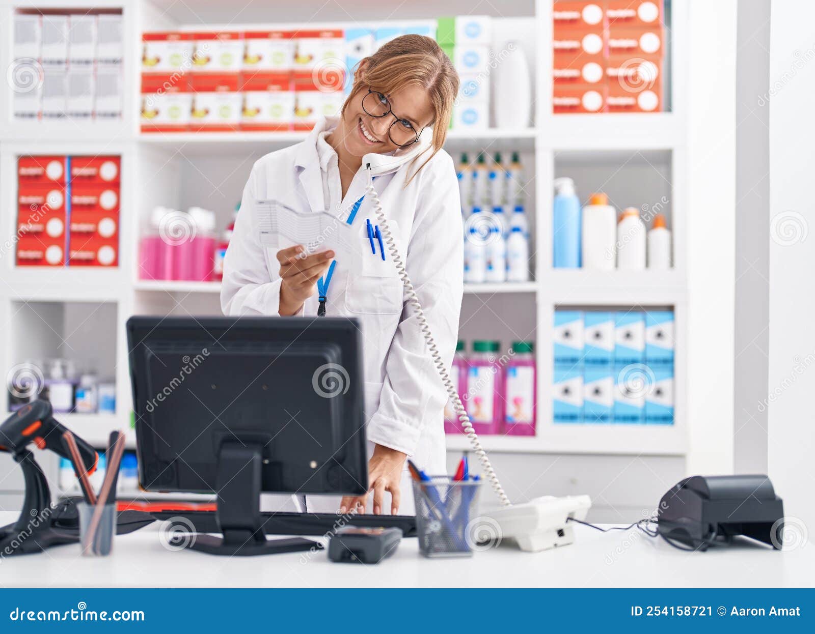 Young Blonde Girl Pharmacist Talking on Telephone Using Computer at ...