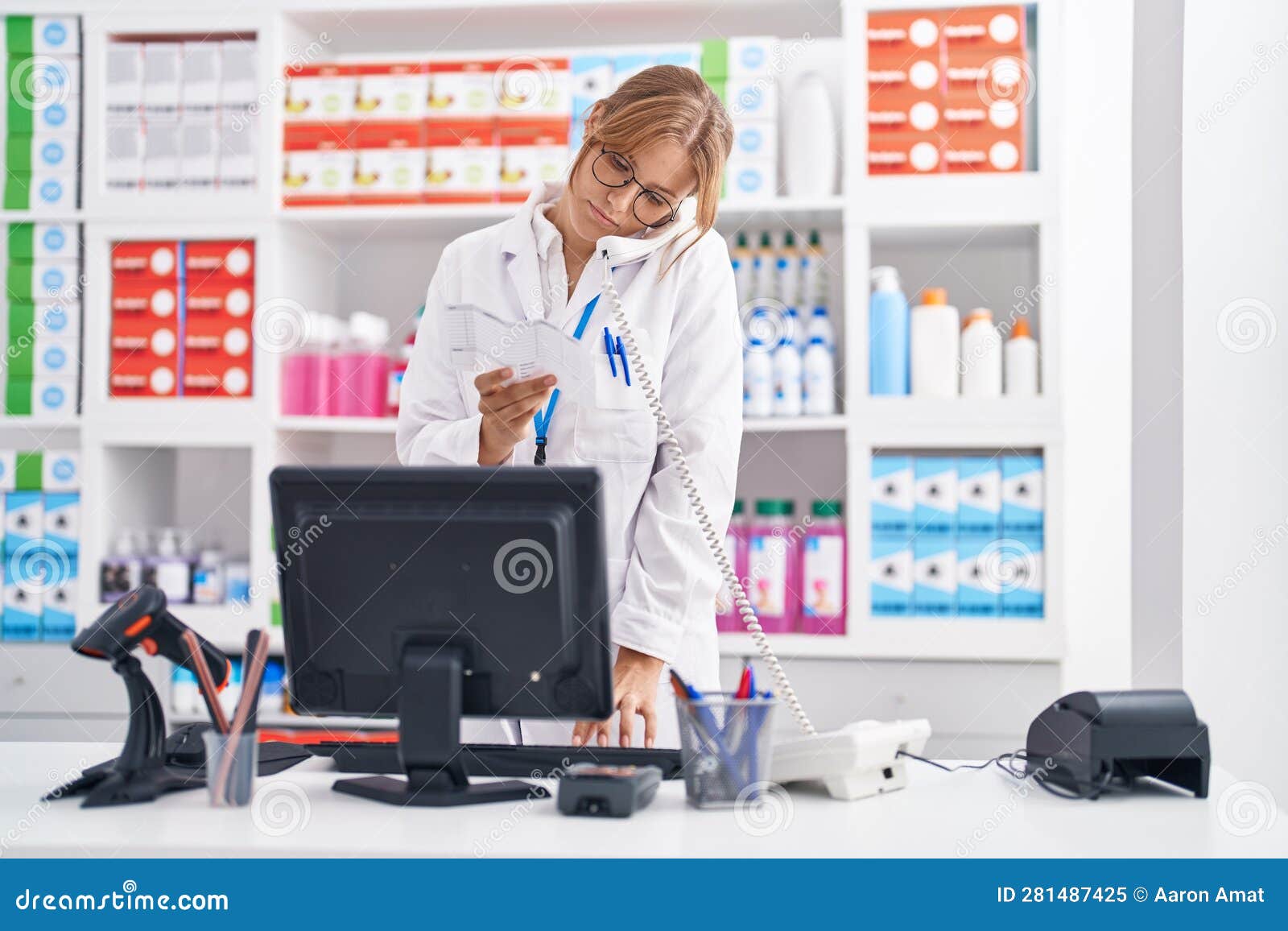 Young Blonde Girl Pharmacist Talking on Telephone Using Computer at ...