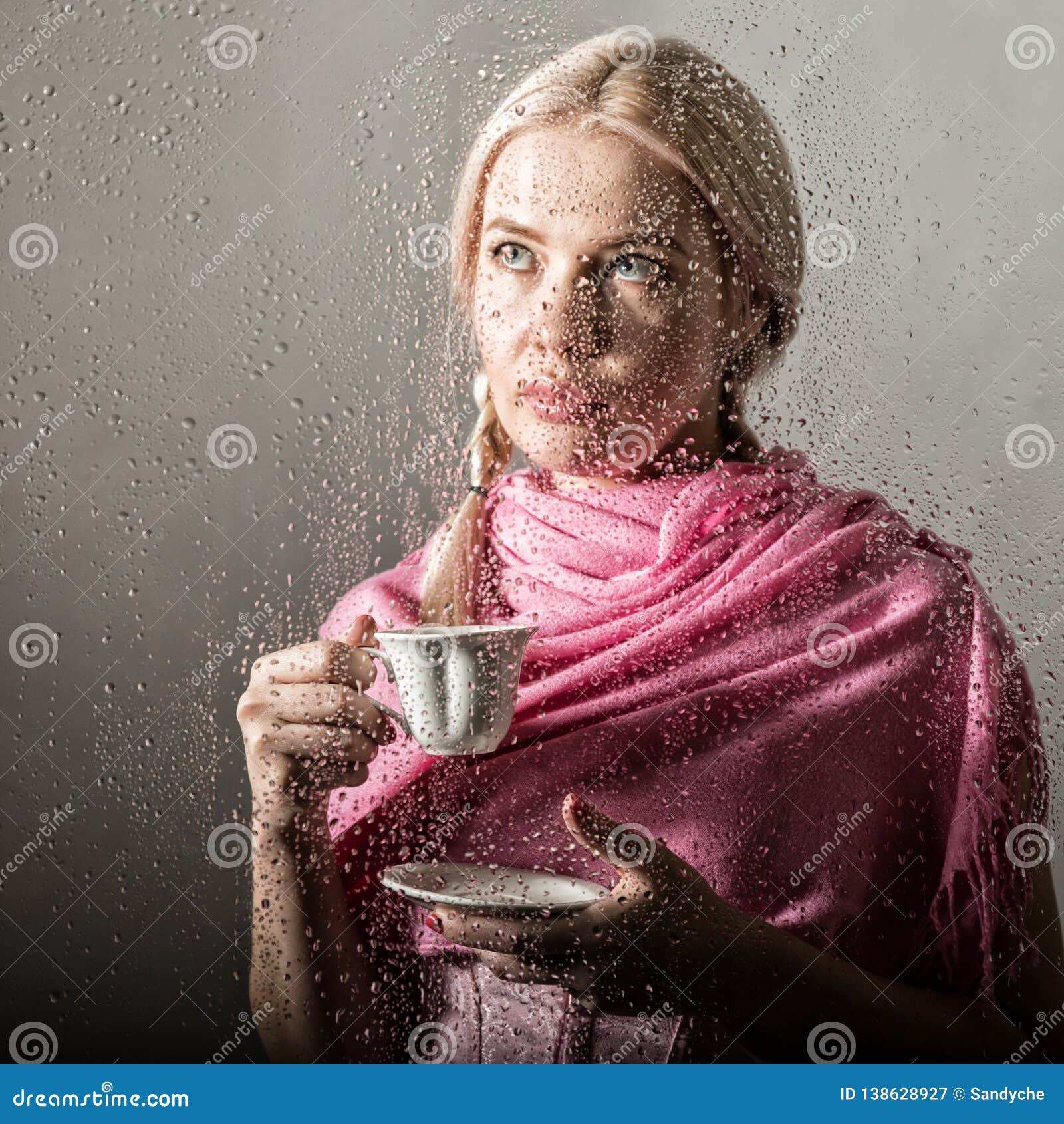 Young Blonde Woman Behind Glass With Water Drops Beautiful Girl Drinks