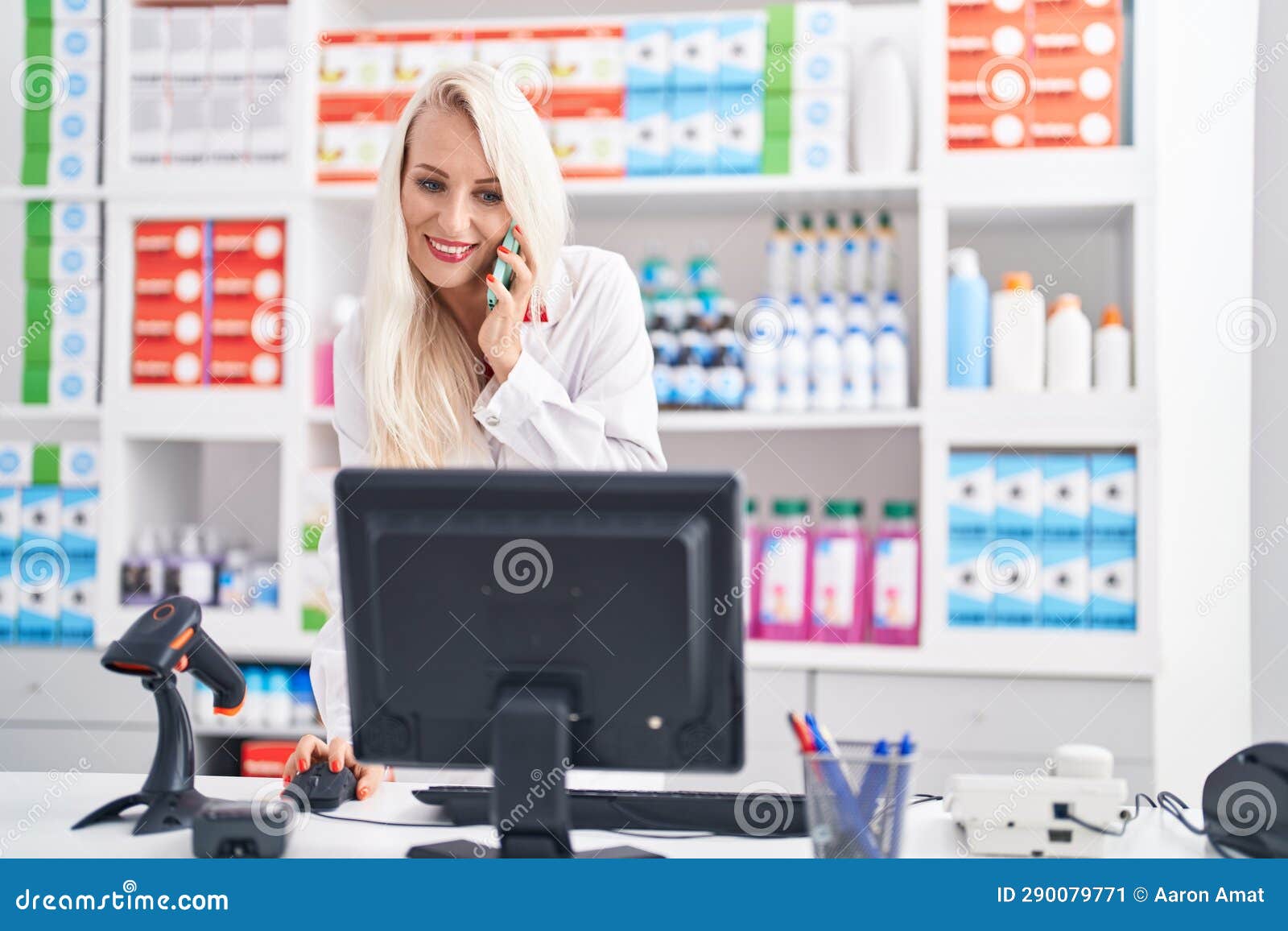 Young Blonde Woman Pharmacist Talking on Smartphone Using Computer at ...