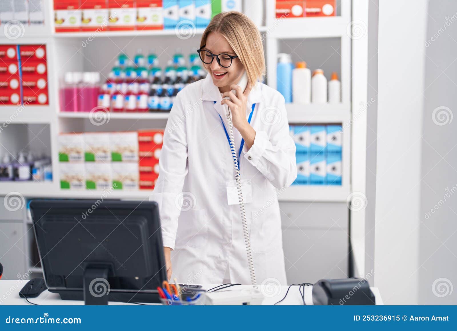 Young Blonde Woman Pharmacist Talking on Telephone Using Computer at ...