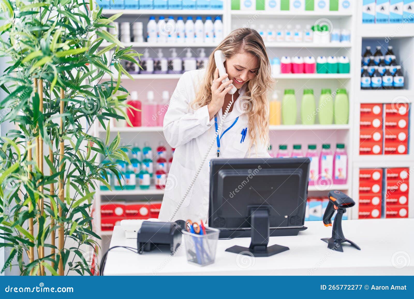 Young Blonde Woman Pharmacist Talking on Telephone Using Computer at ...