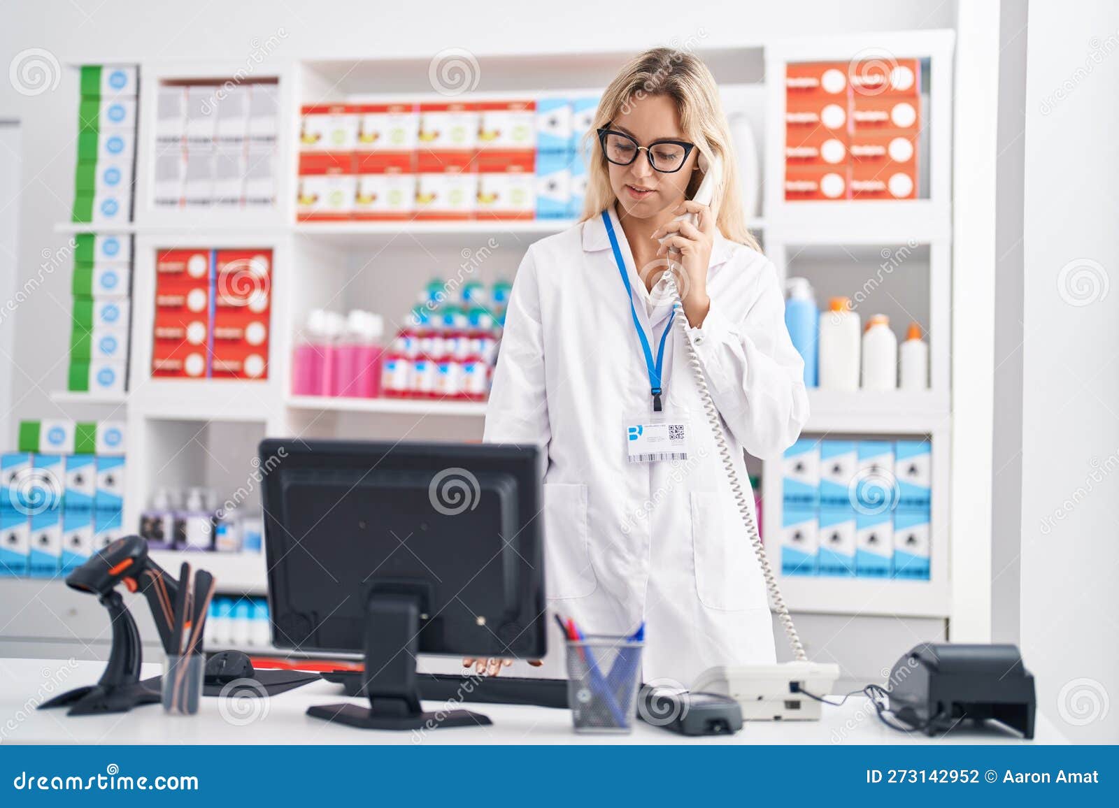 Young Blonde Woman Pharmacist Talking on Telephone Using Computer at ...