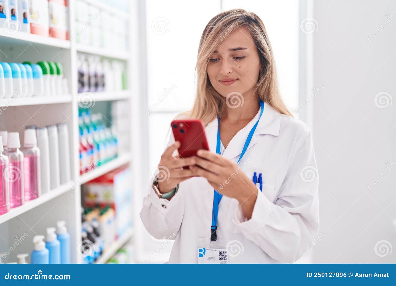 Young Blonde Woman Pharmacist Using Smartphone Working at Pharmacy ...