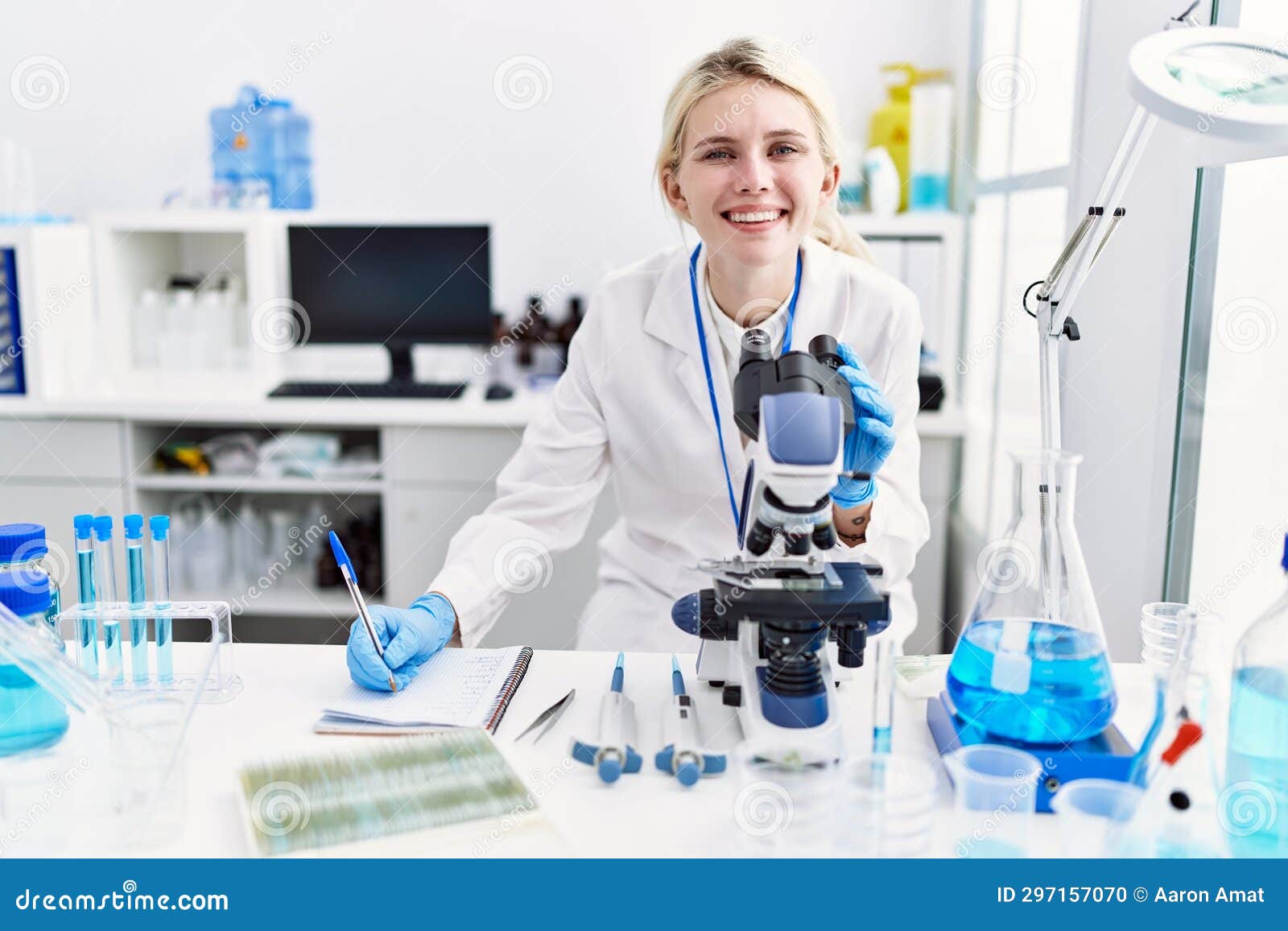 Young Blonde Woman Scientist Using Microscope Taking Notes at ...