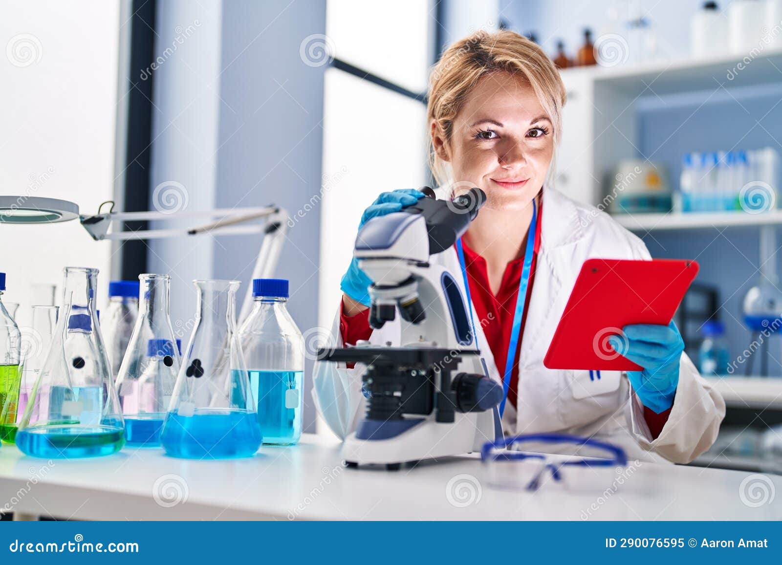 Young Blonde Woman Scientist Using Touchpad and Microscope at ...