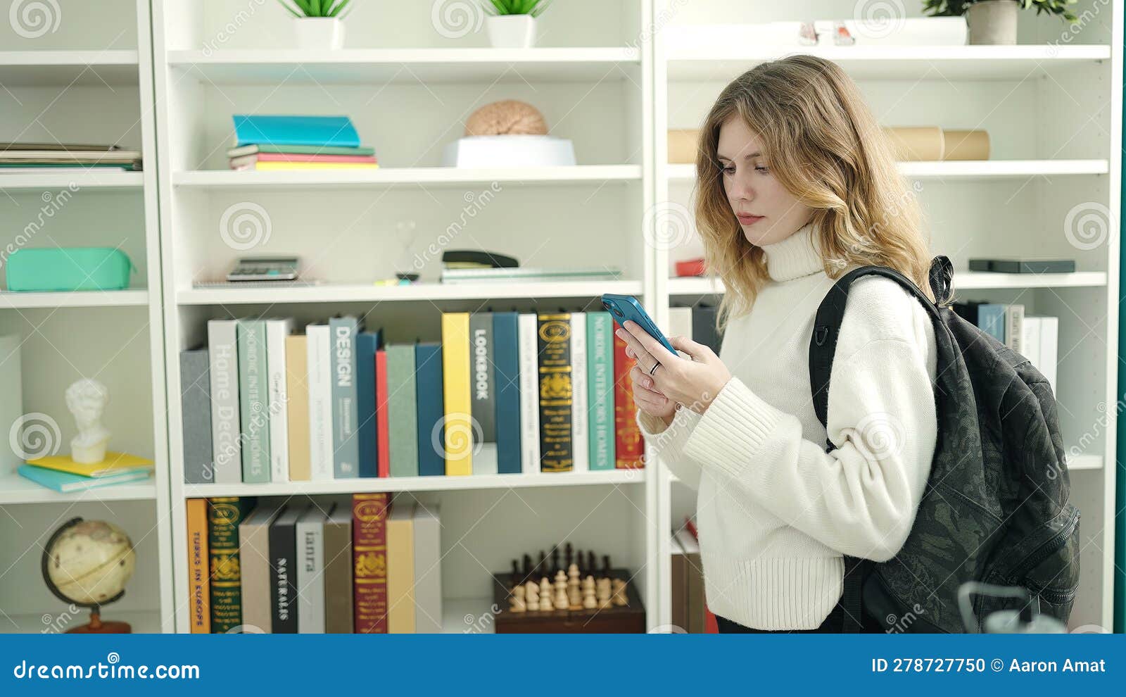 Young Blonde Woman Student Using Smartphone Standing at Library ...