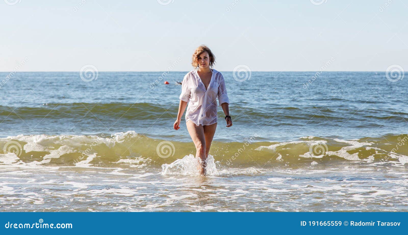 Young Blonde Woman In A Wet White Shirt Comes Out Of The Water Near The