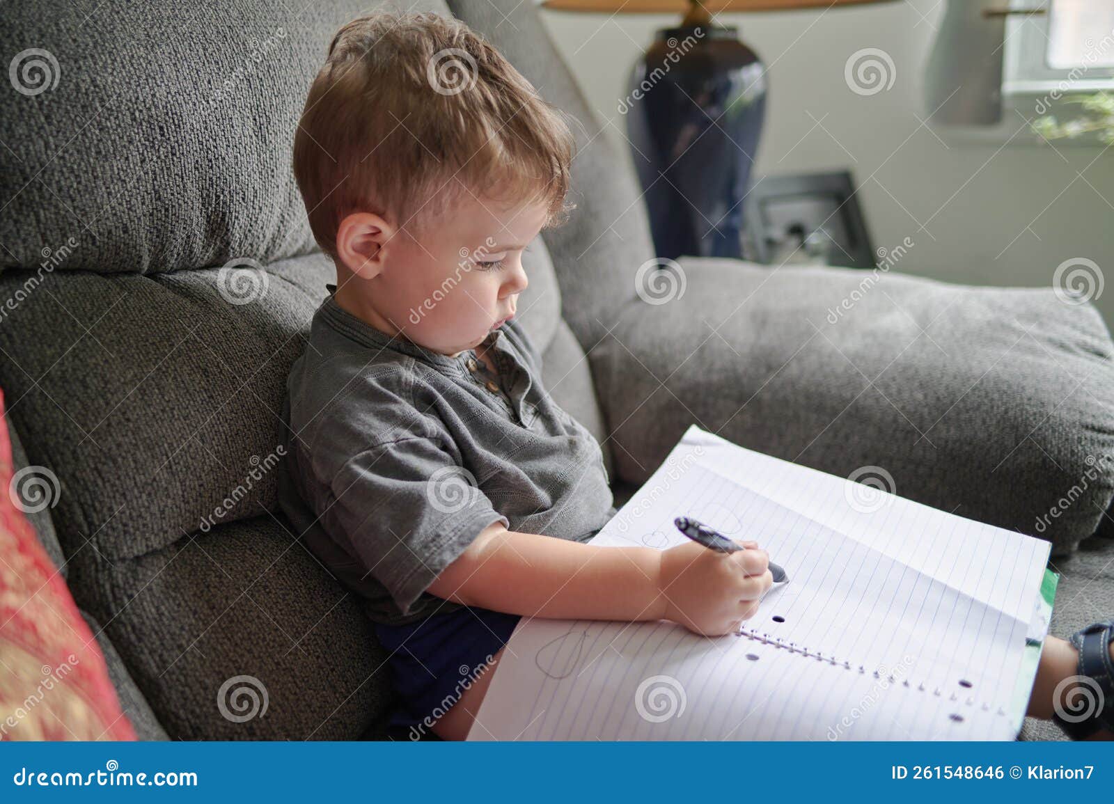 A Young Boy Drawing Doodles in a Notebook while Sitting on a Couch at ...