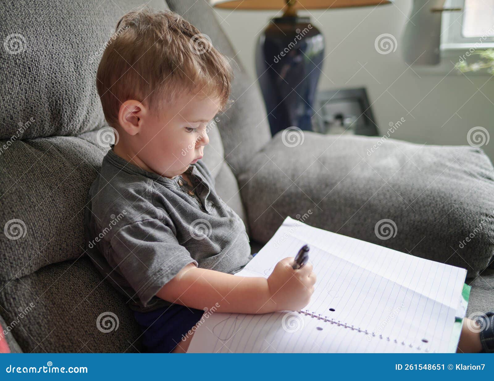 A Young Boy Drawing Doodles in a Notebook while Sitting on a Couch at ...
