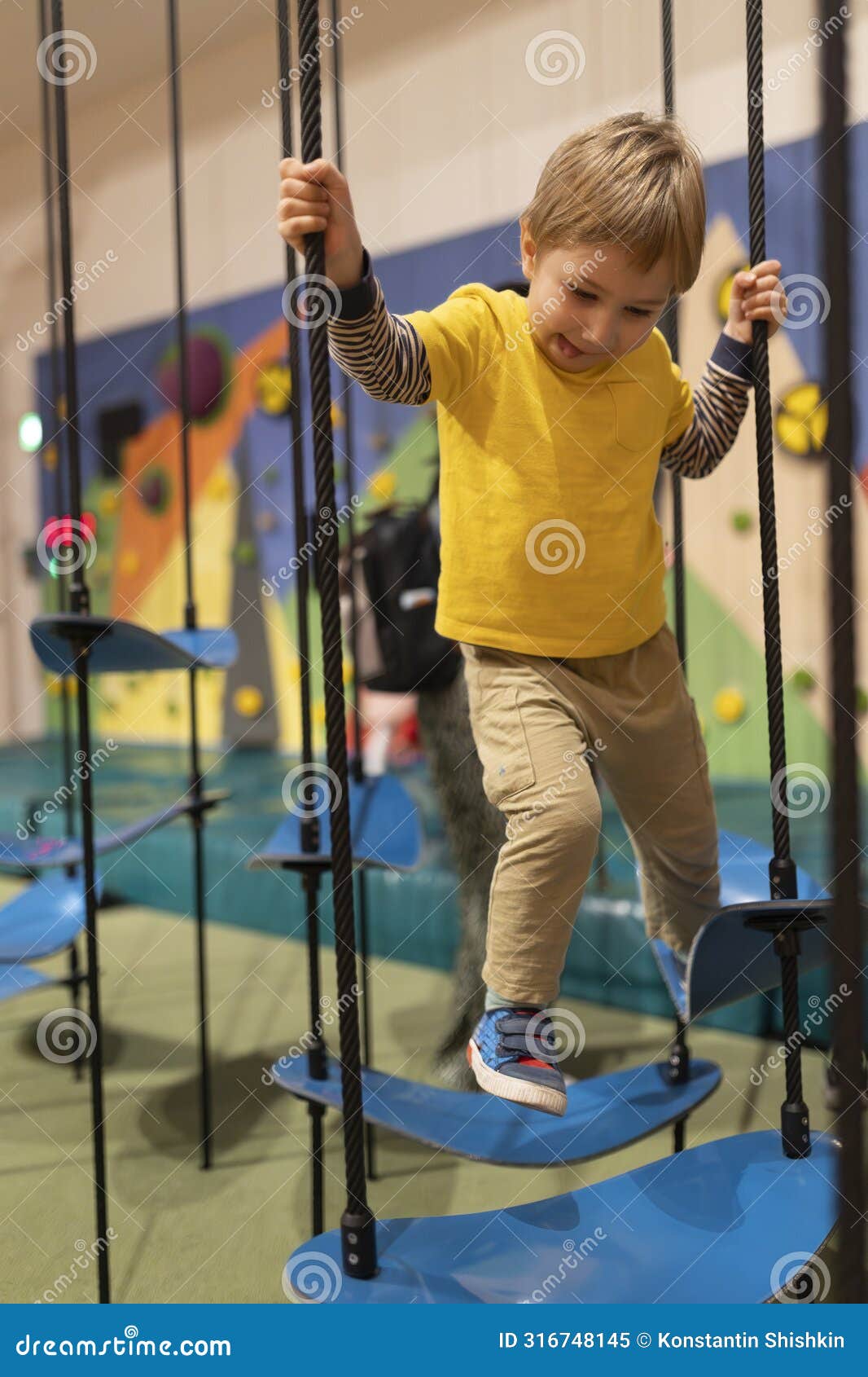 A Young Boy is Hanging from a Rope and Balancing on a Blue Platform ...