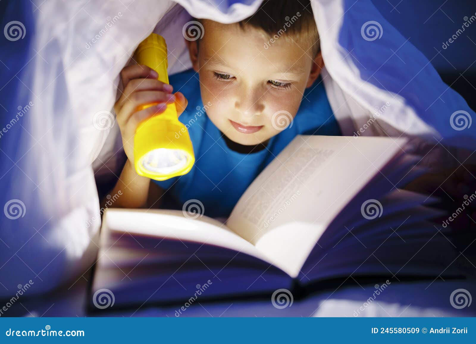 A Young Boy Reading a Book Under the Covers with a Flashlight at Dark ...