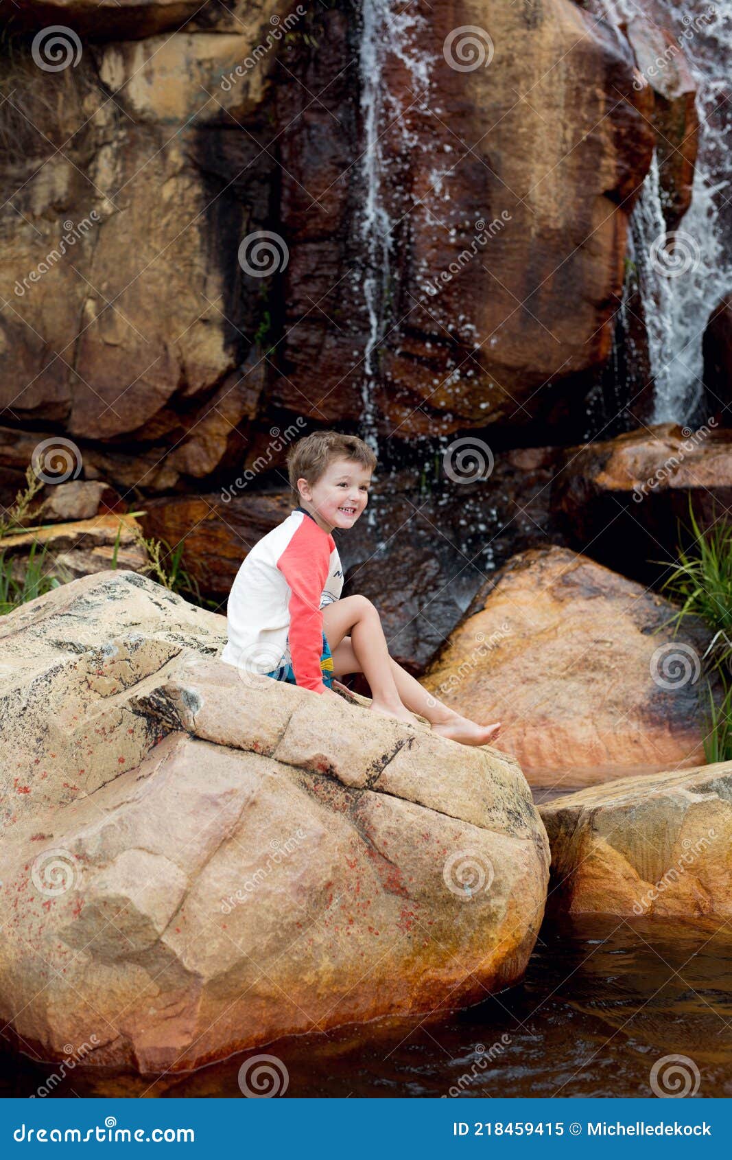 A Young Boy Sitting on a Rock in Front of a Waterfall Stock Image ...