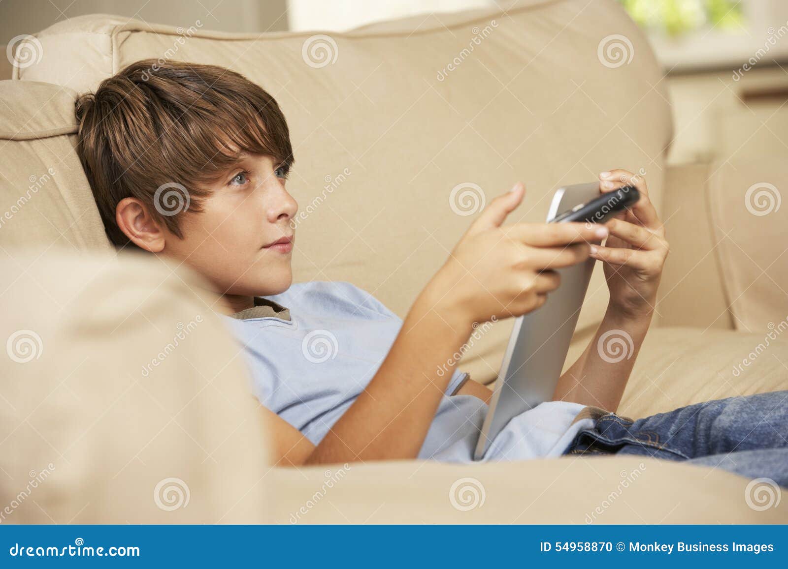 Young Boy Sitting on Sofa at Home Using Tablet Computer Whilst Watching ...