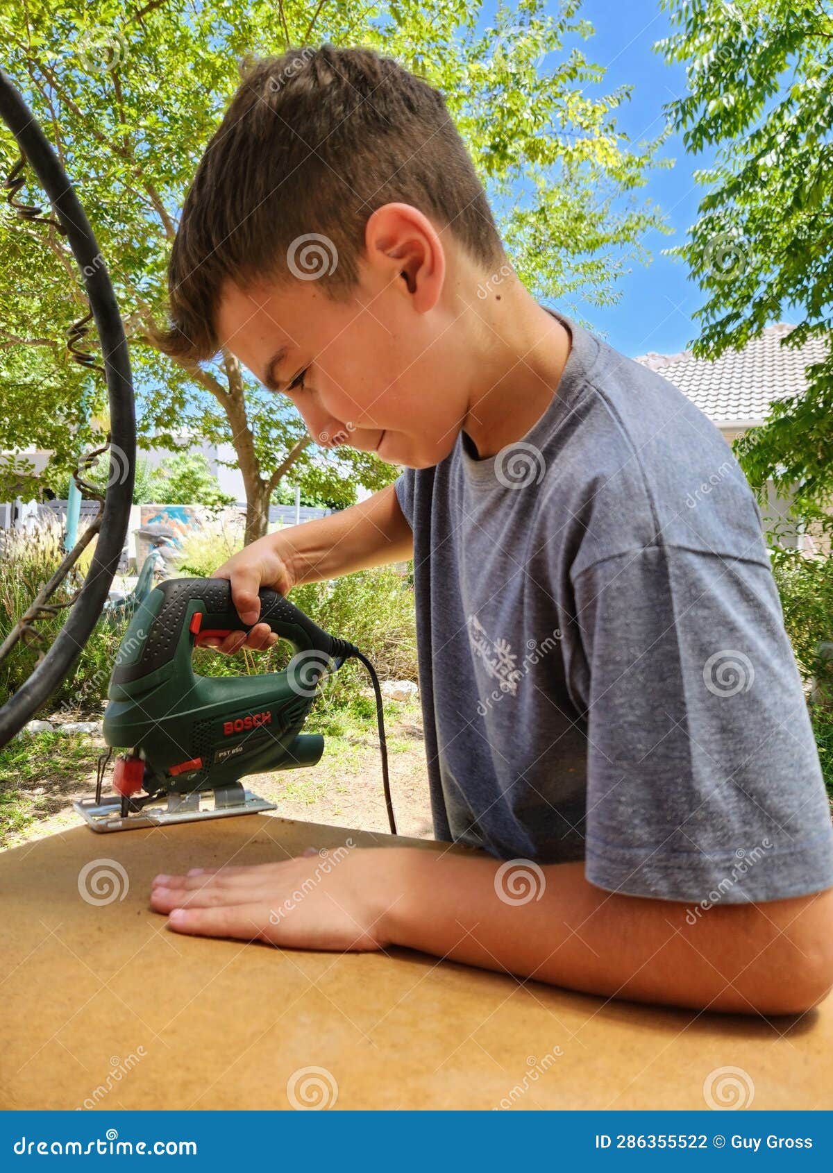 A Young Boy Using an Electric Jig Saw in the Garden. Stock Photo ...