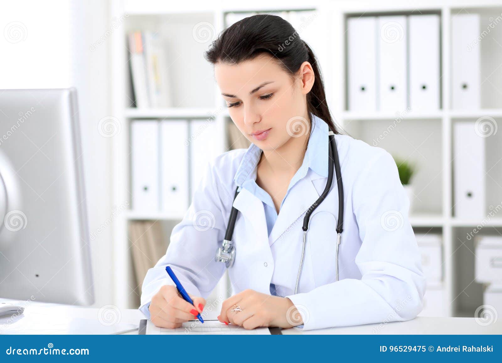 Young Brunette Female Doctor Sitting At The Table And Working By