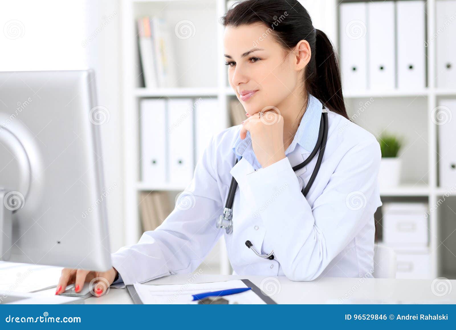 Young Brunette Female Doctor Sitting At The Table And Working By
