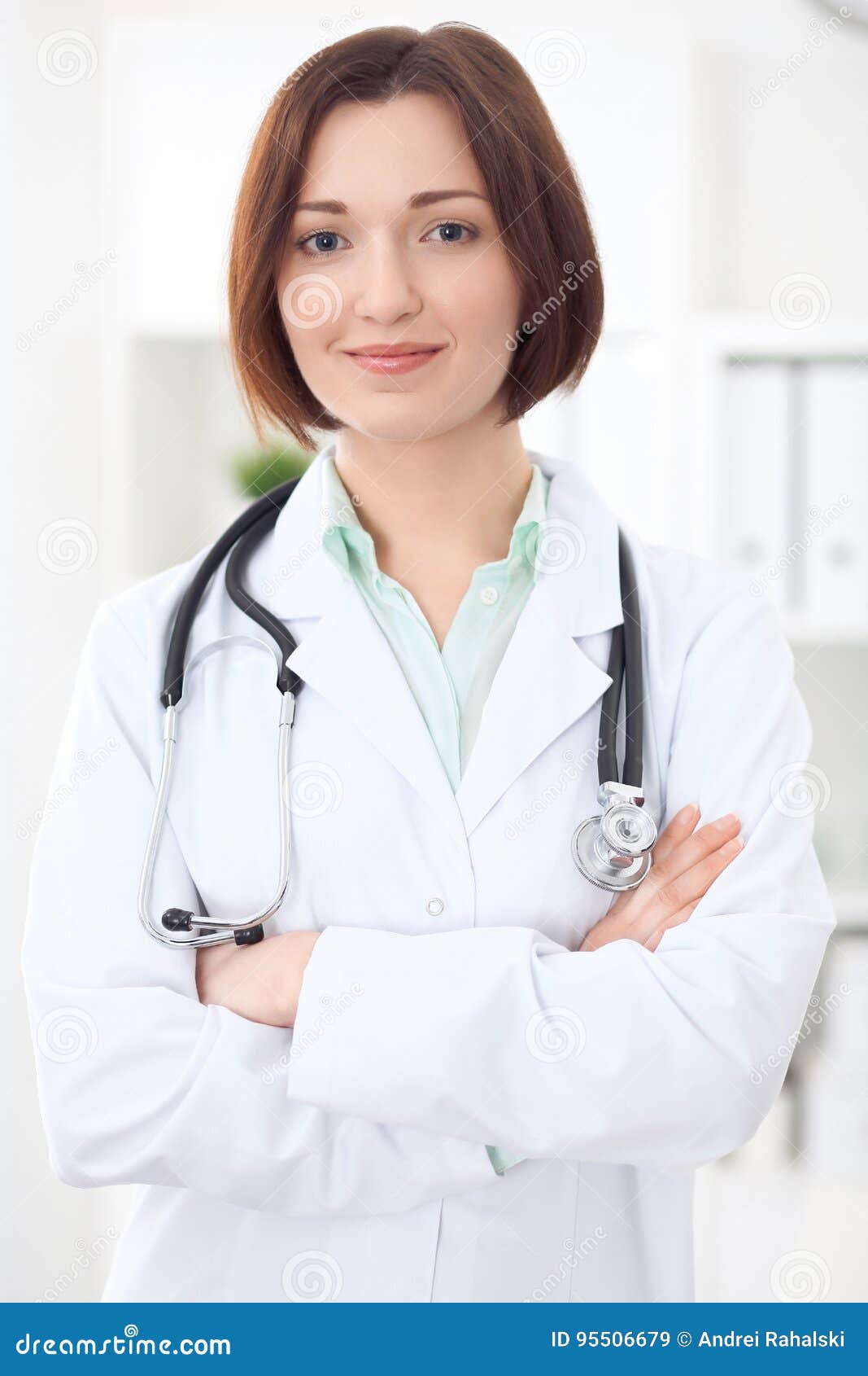 Young Brunette Female Doctor Standing With Arms Crossed And Smiling At