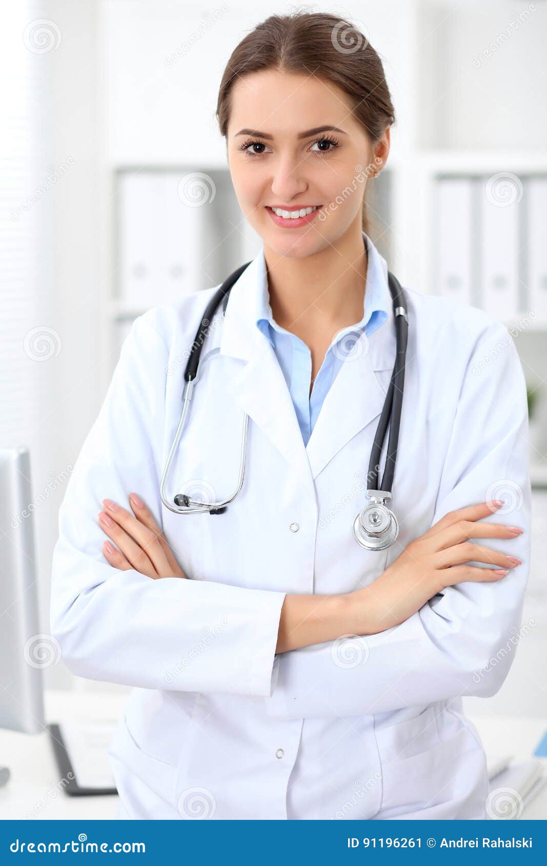 Young Brunette Female Doctor Standing With Arms Crossed And Smiling At