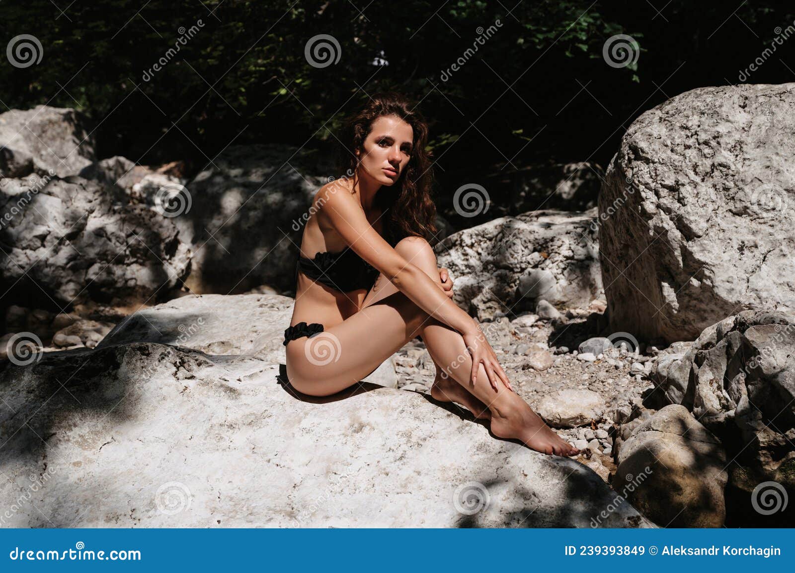 Young Brunette Girl In Black Swimsuit Poses Sexually On The Rocks By