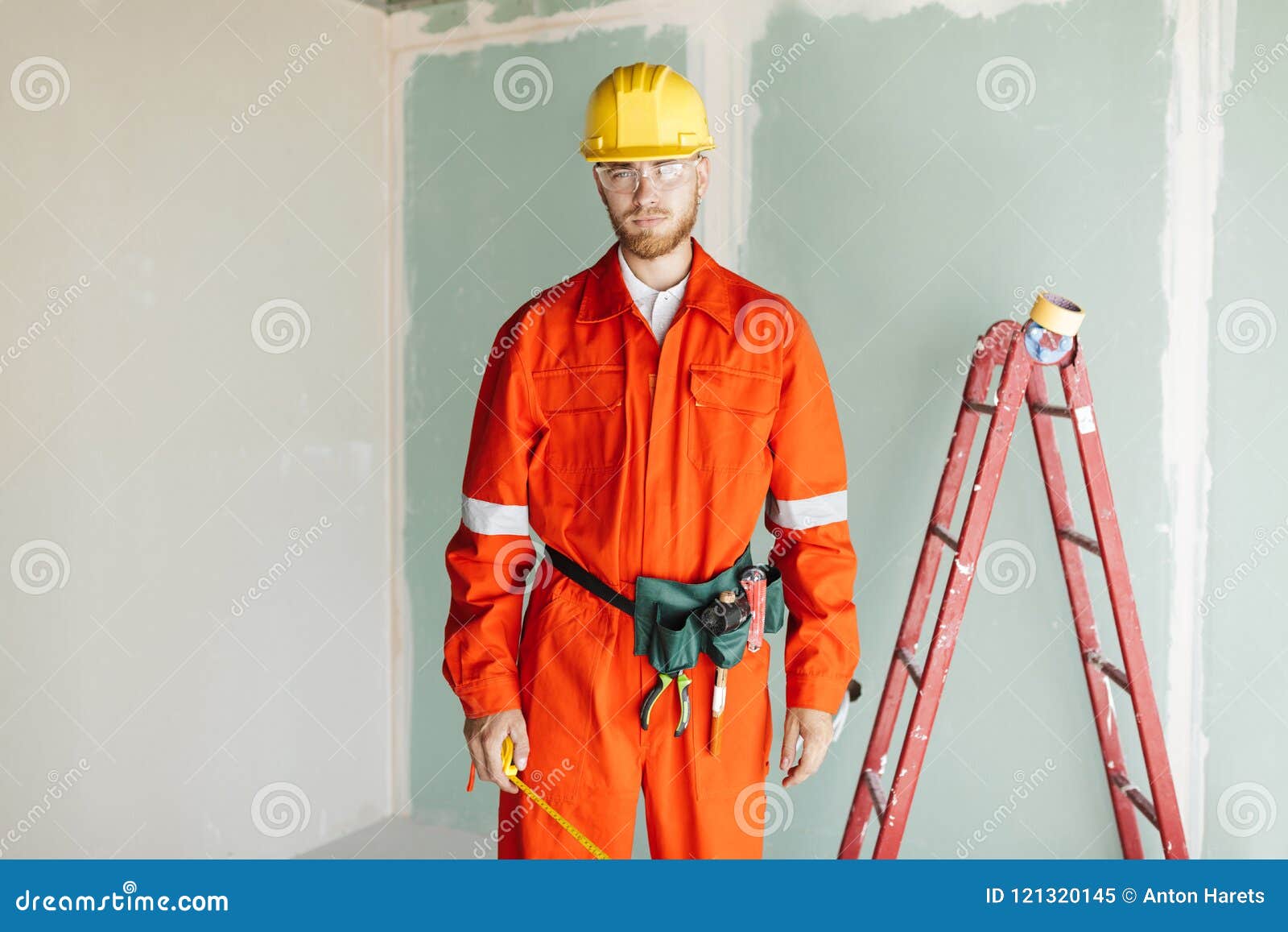 Young Builder in Orange Work Clothes and Hardhat Holding Roulett Stock ...