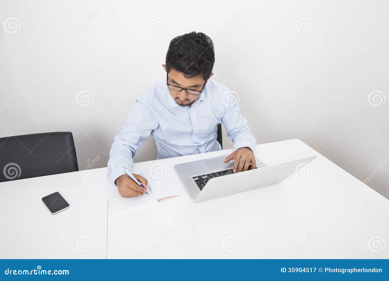 Young Businessman Writing while Using Laptop at Desk in Office Stock ...