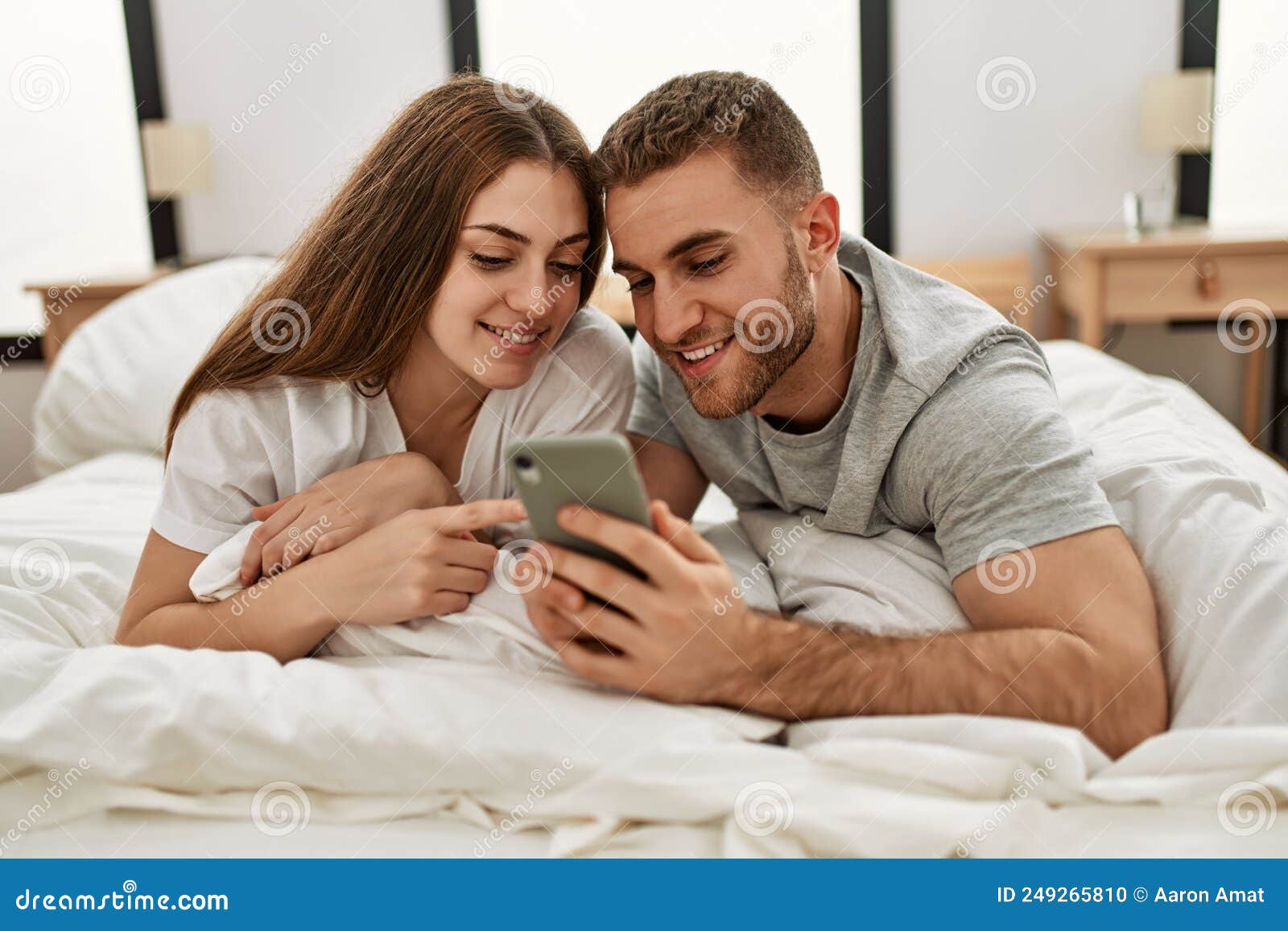 Young Caucasian Couple Using Smartphone Lying on Bed at Home Stock Photo - Image of happy ...