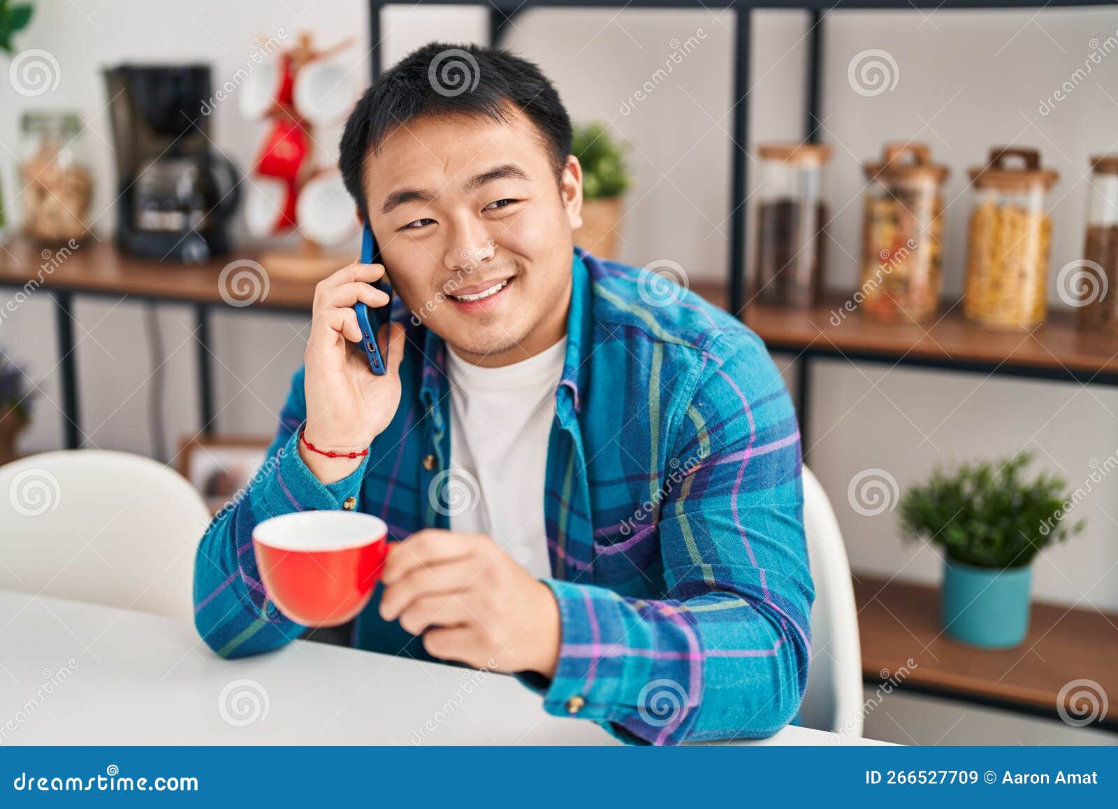 Young Chinese Man Drinking Coffee and Talking on the Smartphone at Home ...