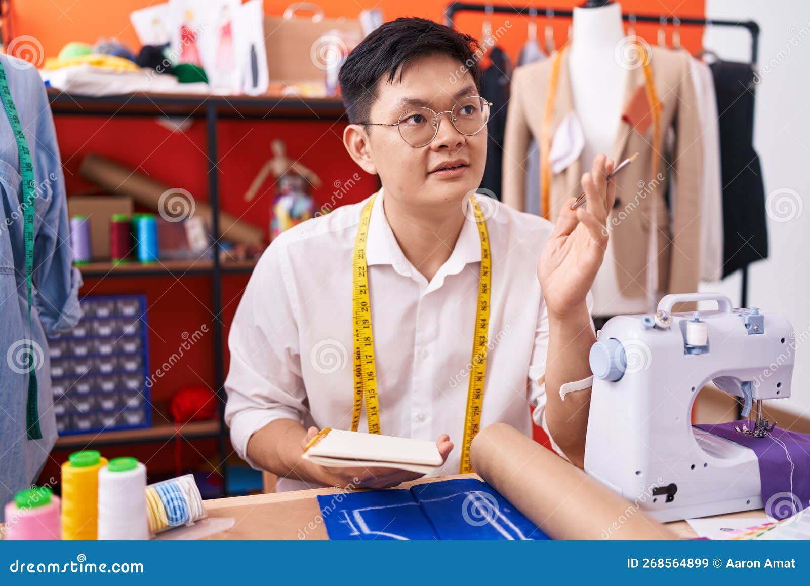 Young Chinese Man Tailor Sitting on Table Speaking at Atelier Stock ...