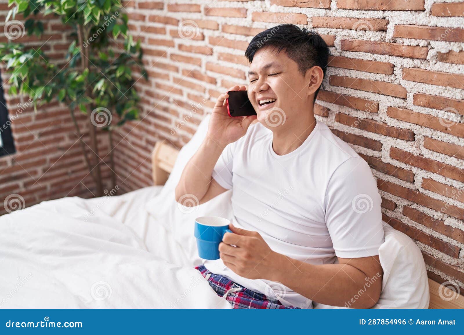 Young Chinese Man Talking on Smartphone Drinking Coffee at Bedroom ...