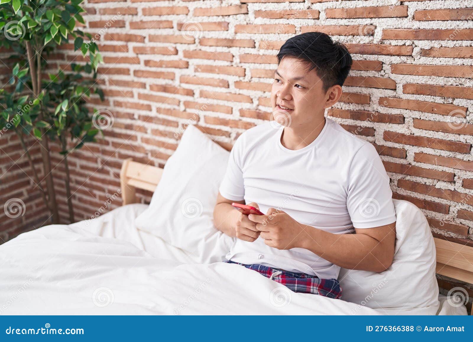 Young Chinese Man Using Smartphone Sitting on Bed at Bedroom Stock ...