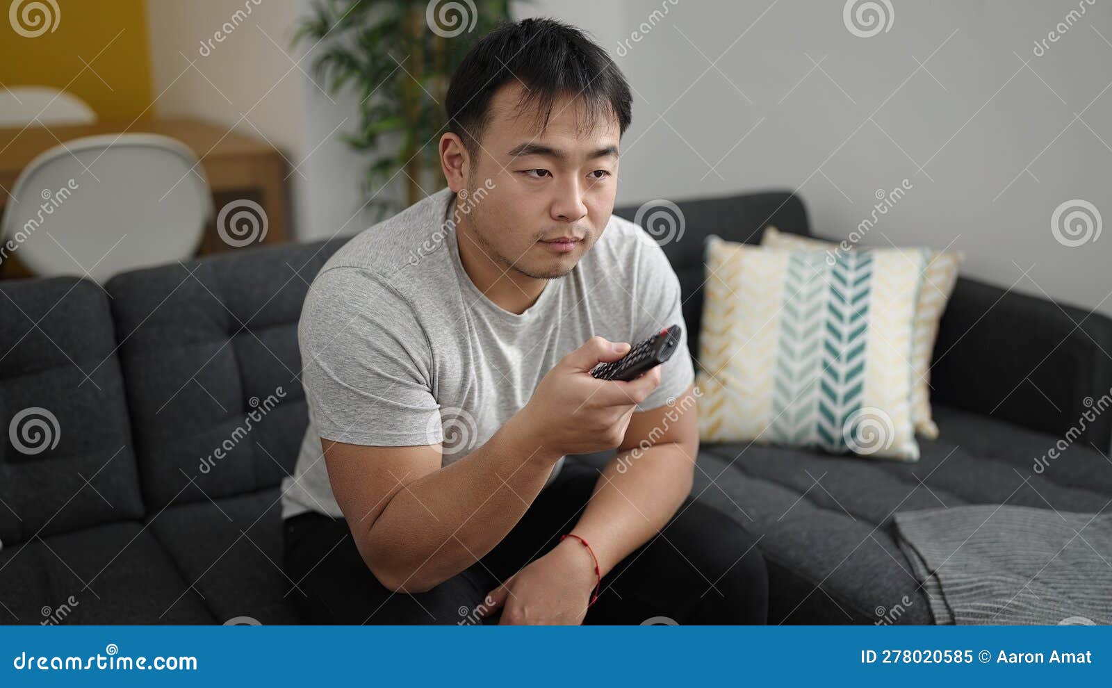 Young Chinese Man Watching Tv Sitting on Sofa with Boring Expression at ...